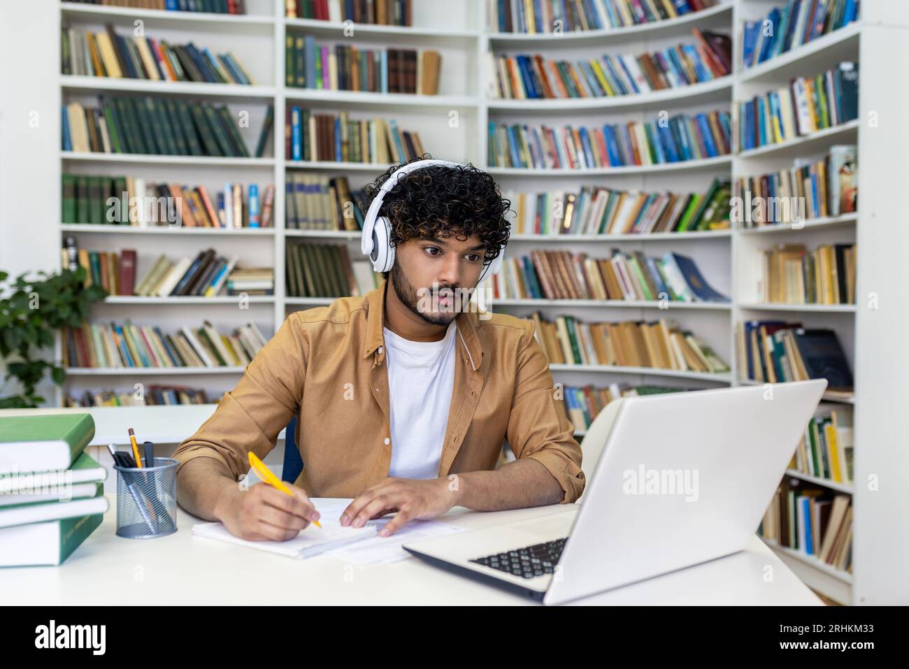 Serious concentrated man in headphones studying in library, hispanic ...