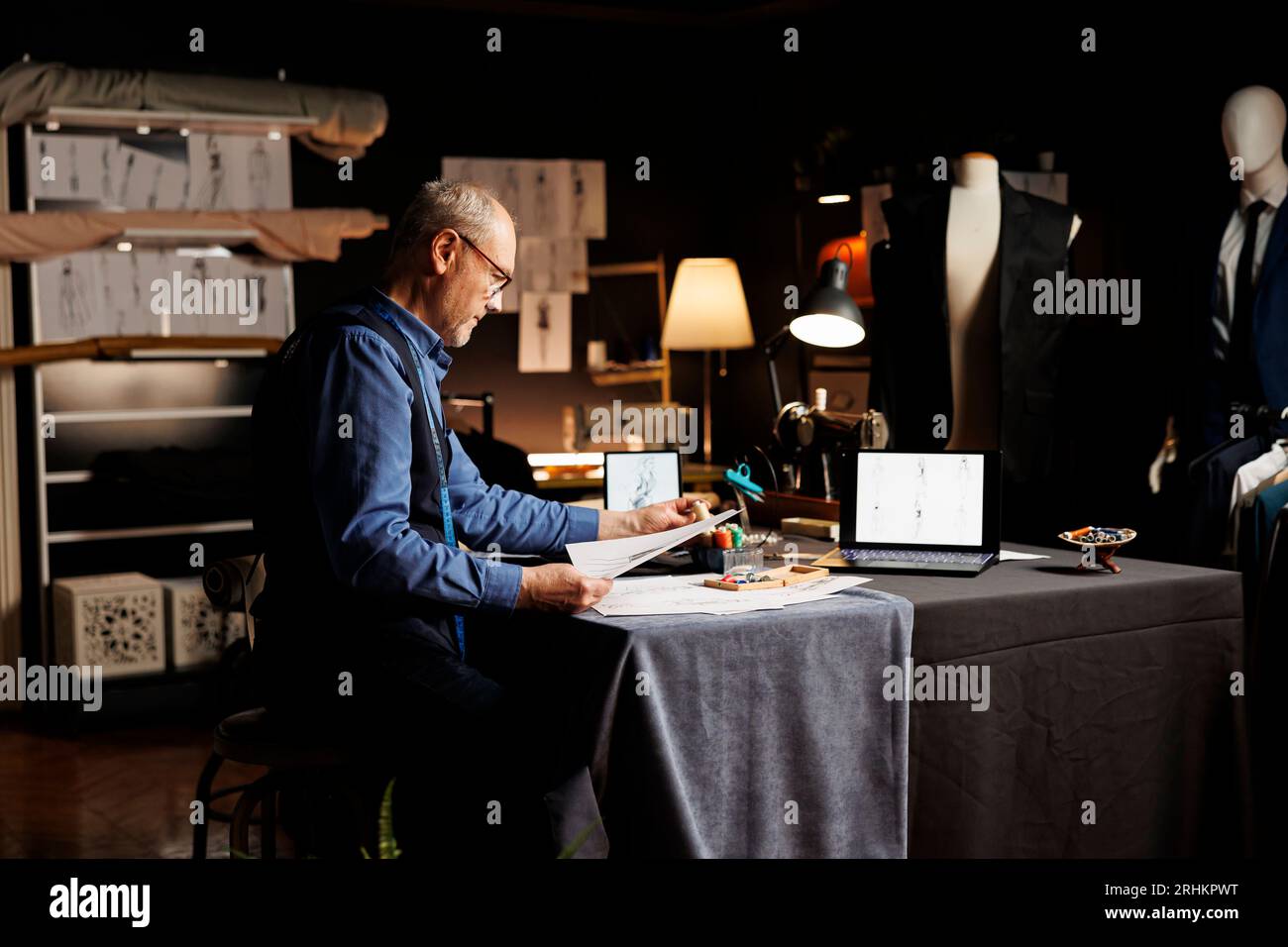 Elderly fashion designer picking sewing materials and handdrawn ...