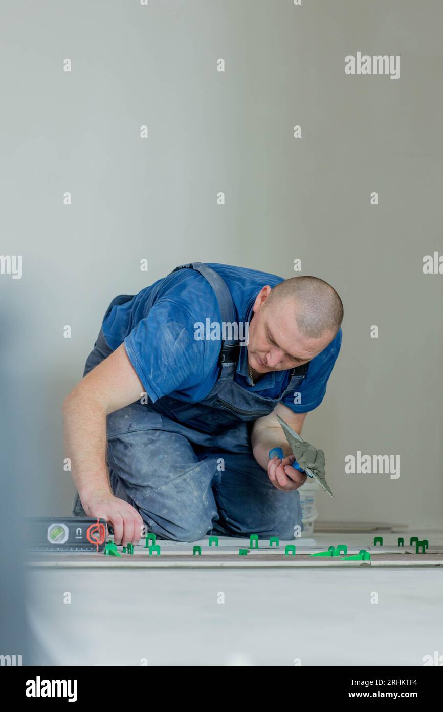 Tiler placing ceramic wall tile in position over adhesive with lash ...