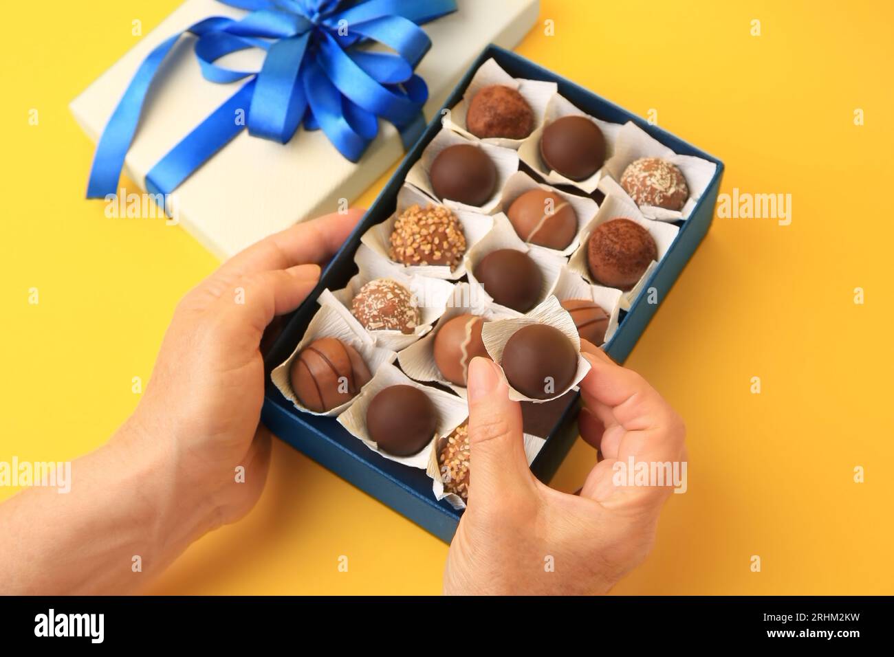 Woman taking chocolate candy from box on yellow background, closeup ...