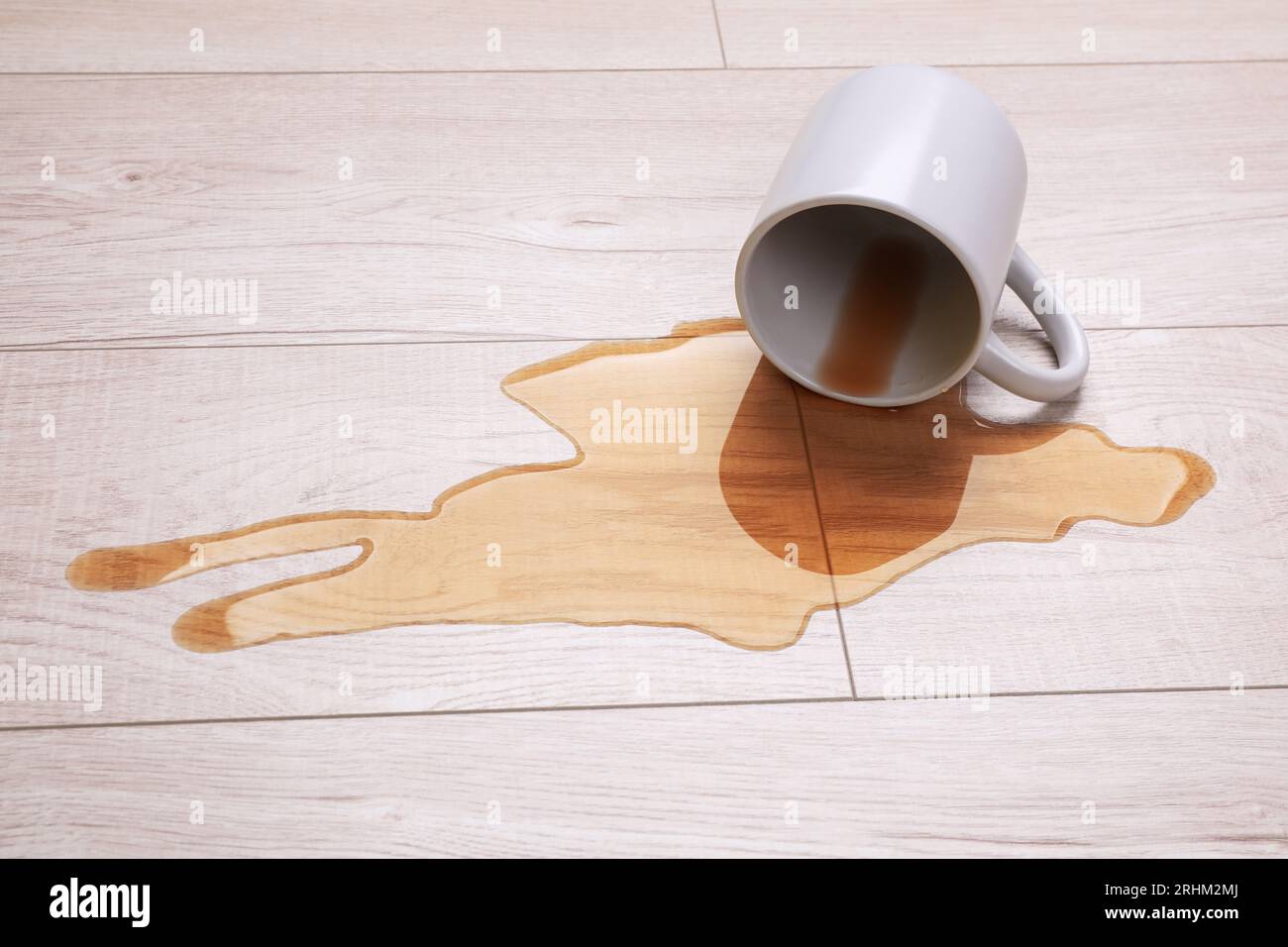 White mug with spilled liquid on wooden floor Stock Photo - Alamy