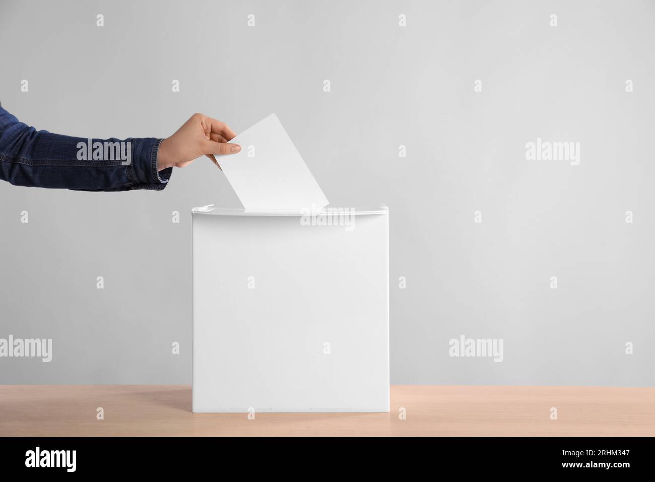 Woman putting her vote into ballot box on wooden table against light ...