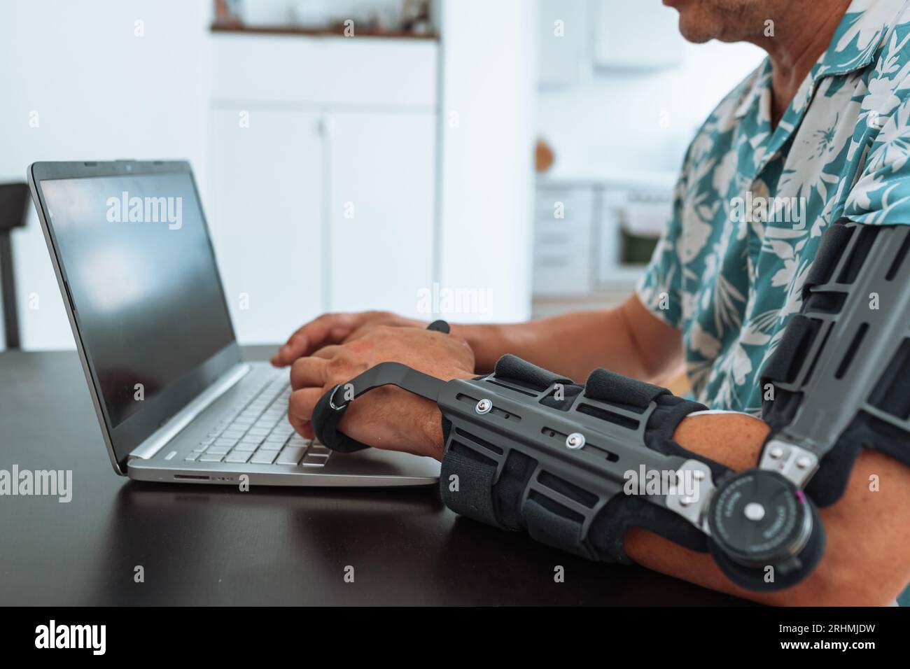 Man with adjustable articulated elbow orthosis typing on laptop ...