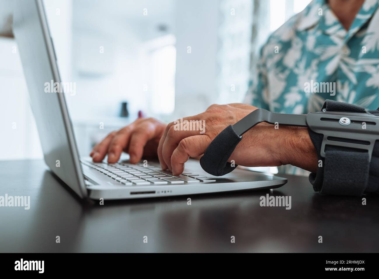 Man with adjustable articulated elbow orthosis typing on laptop ...