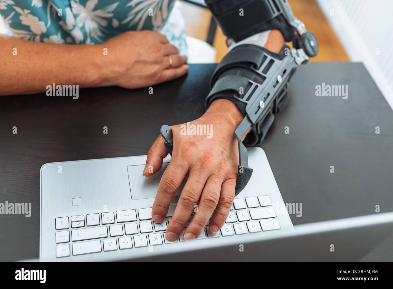 Man with adjustable articulated elbow orthosis typing on laptop ...