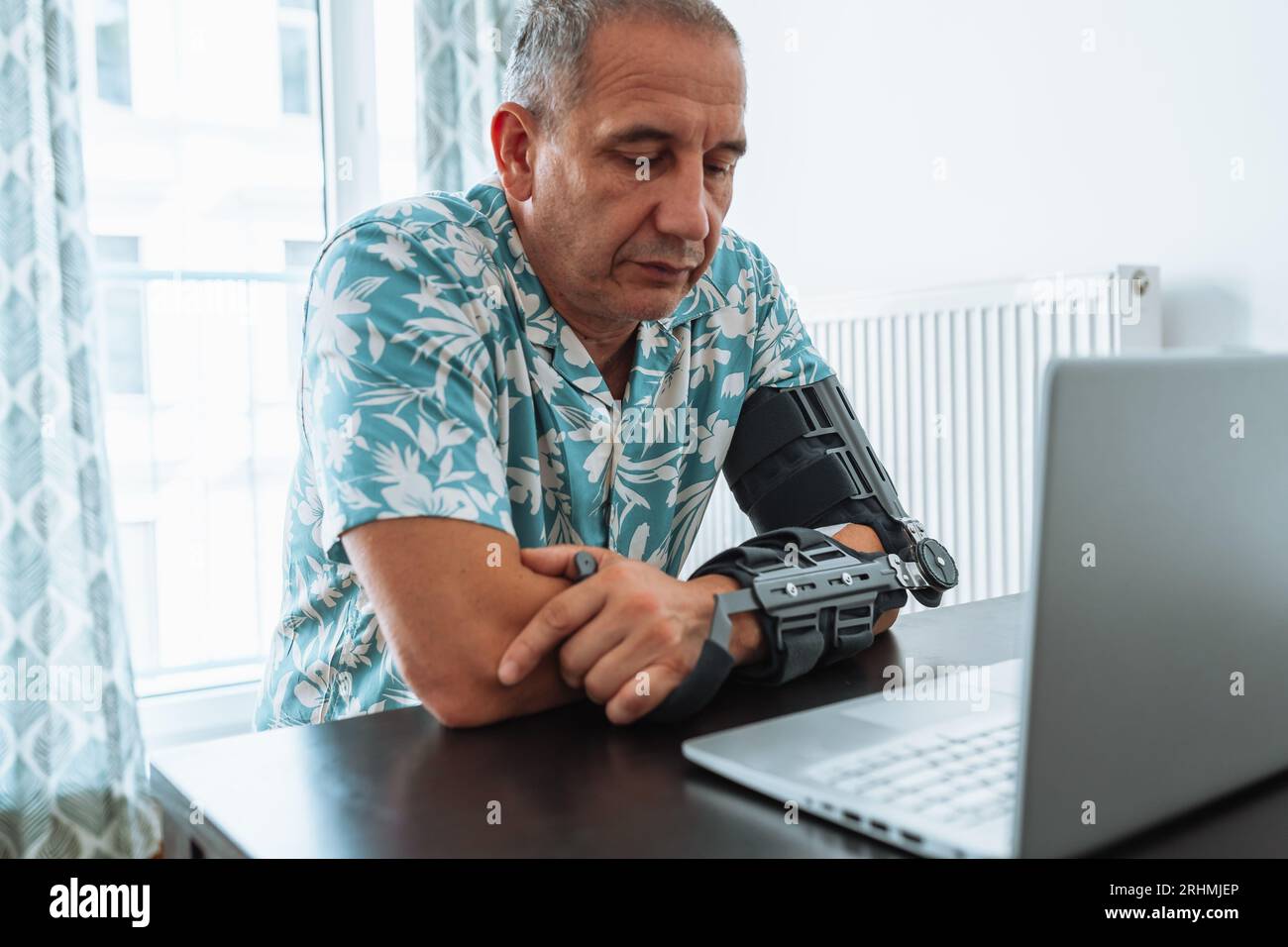 Man with adjustable articulated elbow orthosis typing on laptop ...