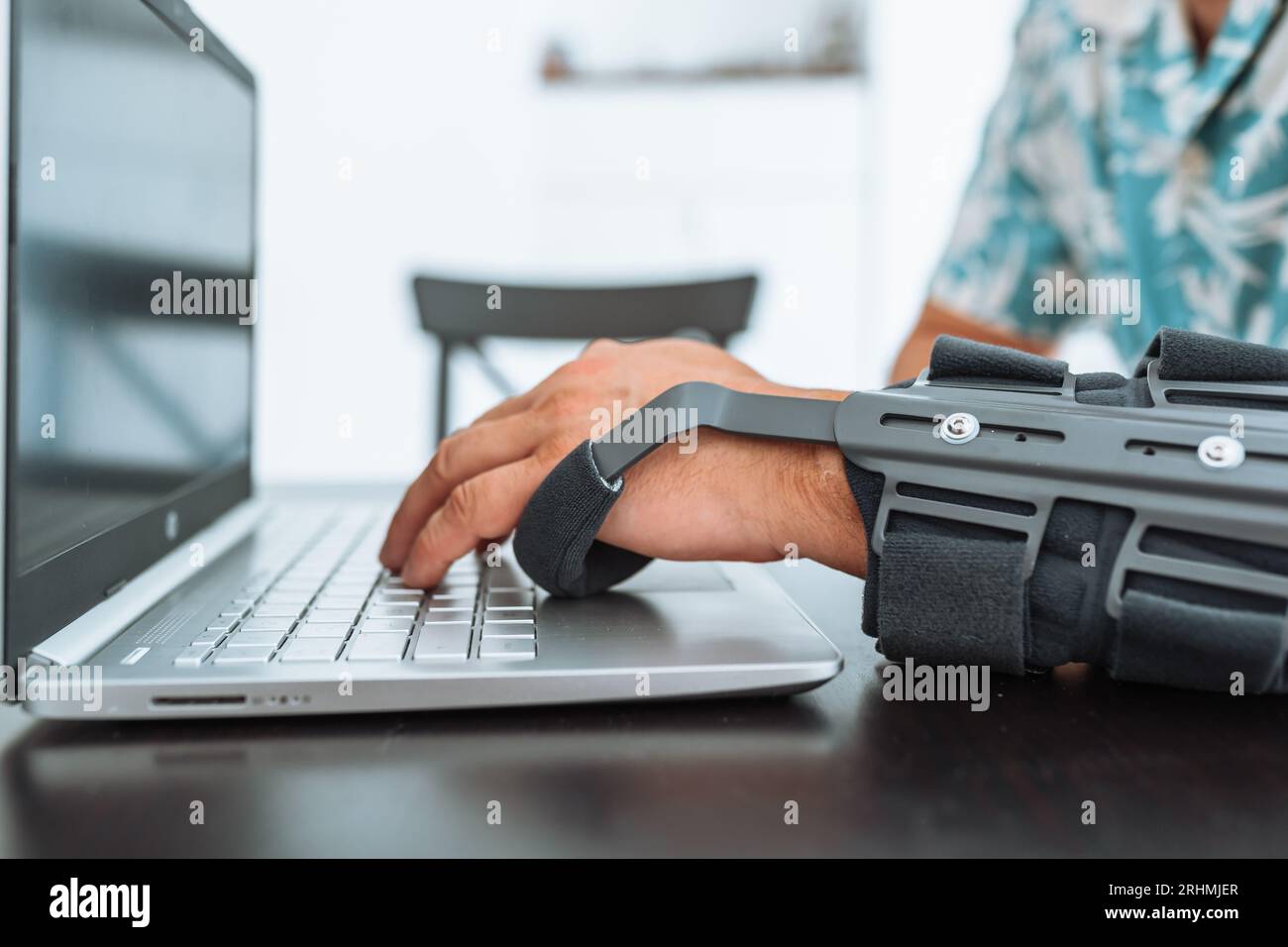 Man with adjustable articulated elbow orthosis typing on laptop ...