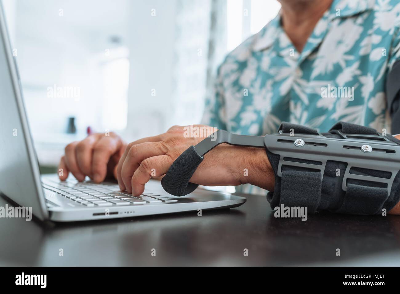 Man with adjustable articulated elbow orthosis typing on laptop ...