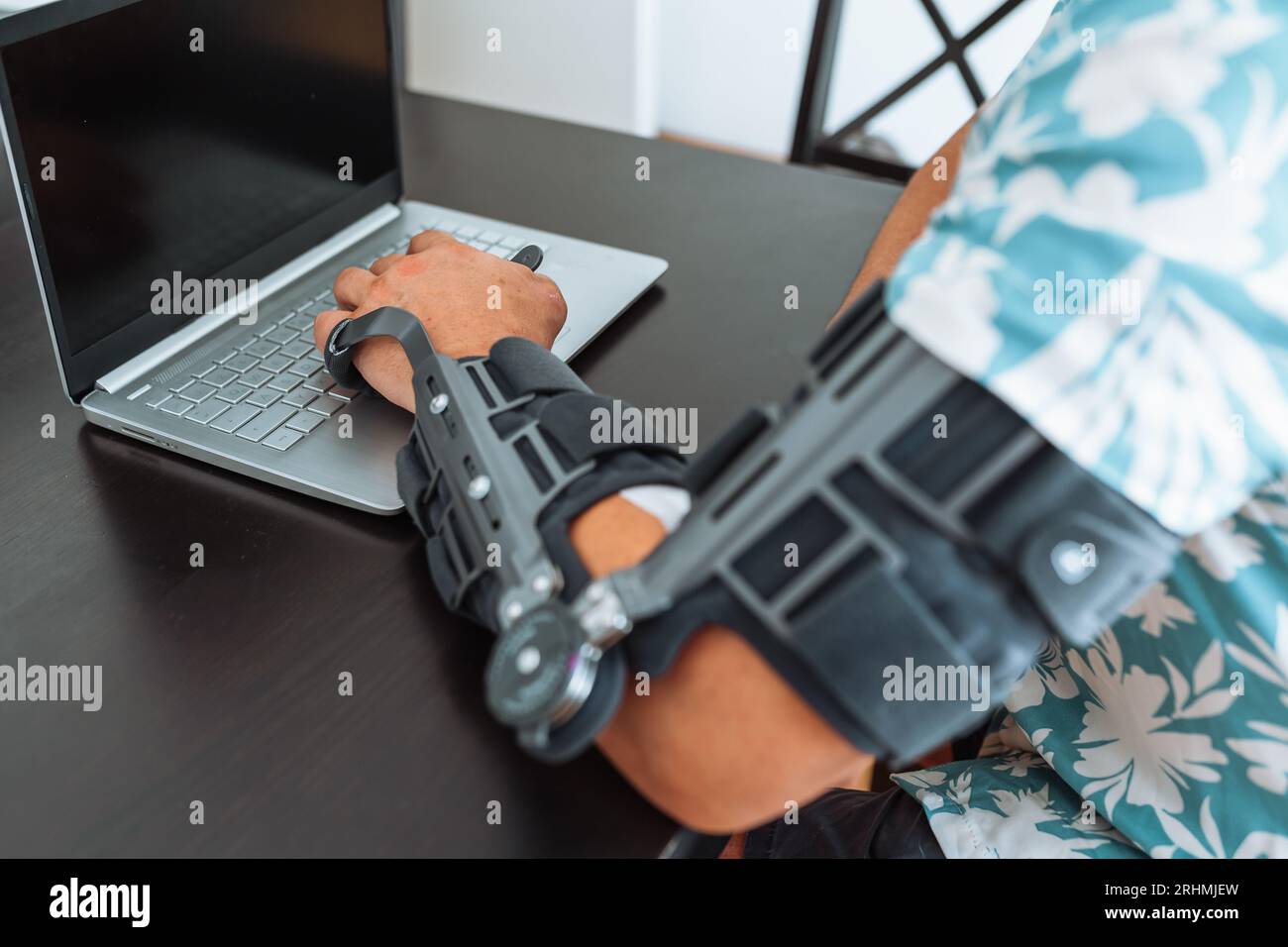 Man with adjustable articulated elbow orthosis typing on laptop ...