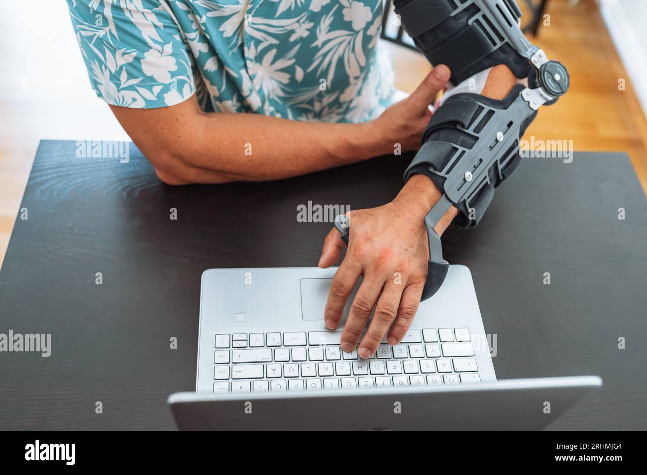 Man with adjustable articulated elbow orthosis typing on laptop ...
