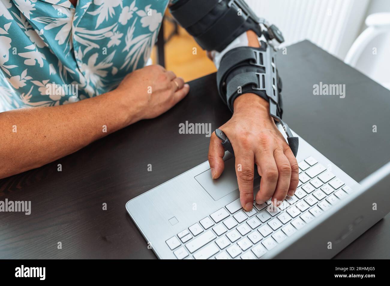 Man with adjustable articulated elbow orthosis typing on laptop ...