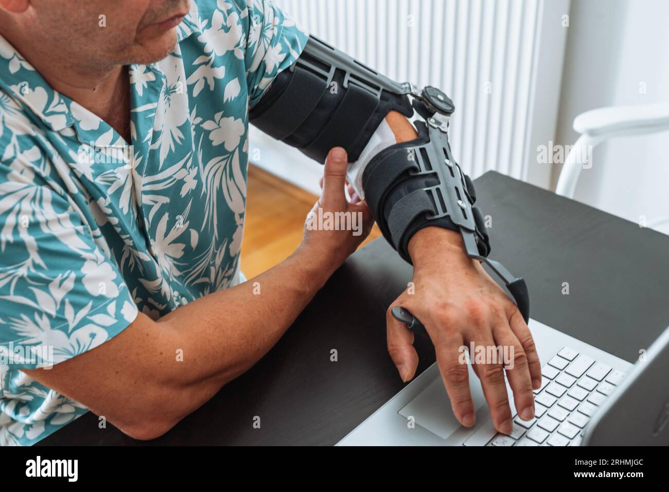 Man with adjustable articulated elbow orthosis typing on laptop ...