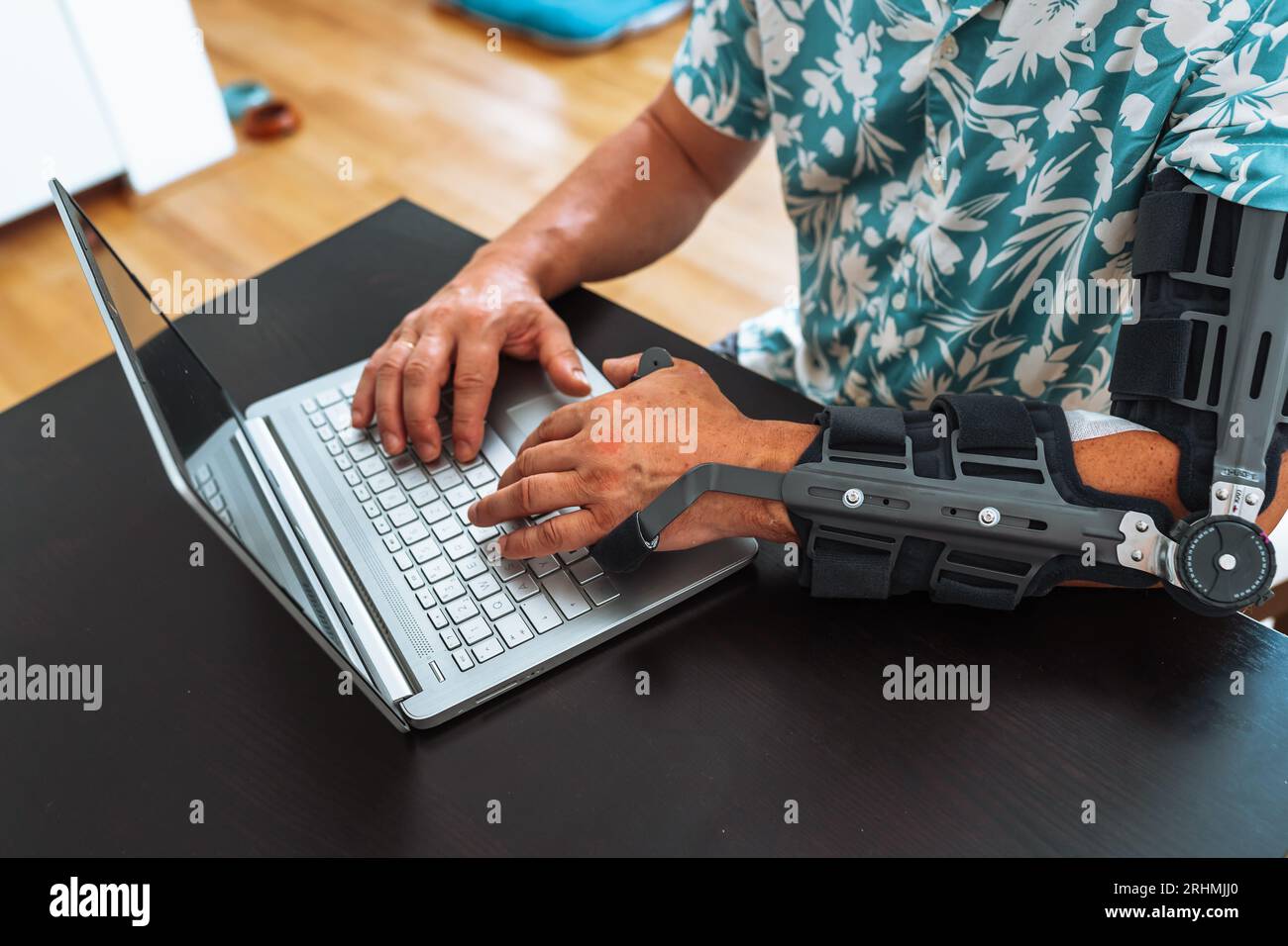 Man with adjustable articulated elbow orthosis typing on laptop ...