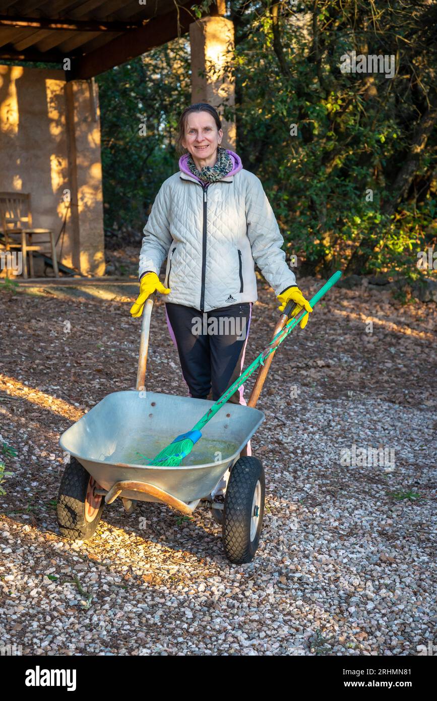 Woman gardening, moving an empty wheelbarrow to collect fallen leaves ...