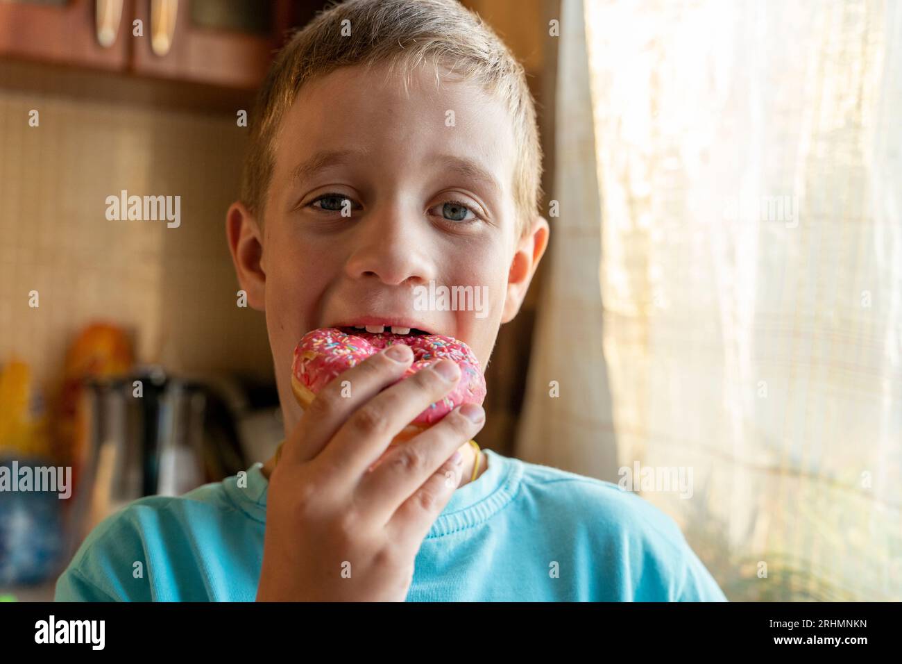 a boy eats a pink donut in the home kitchen. a child is having fun with ...