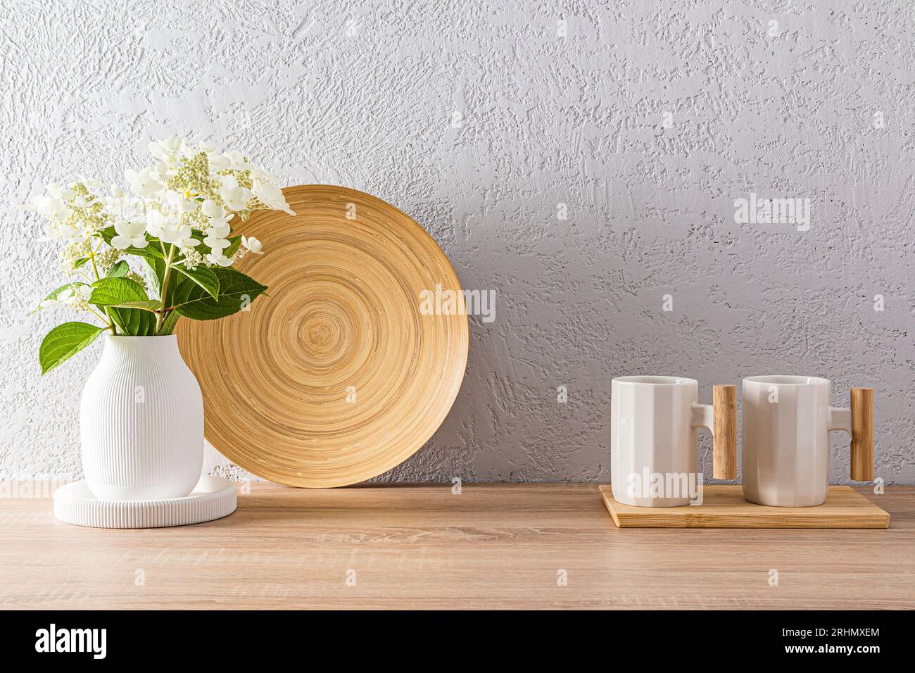 Stylish light kitchen background with two white mugs, a vase of flowers ...