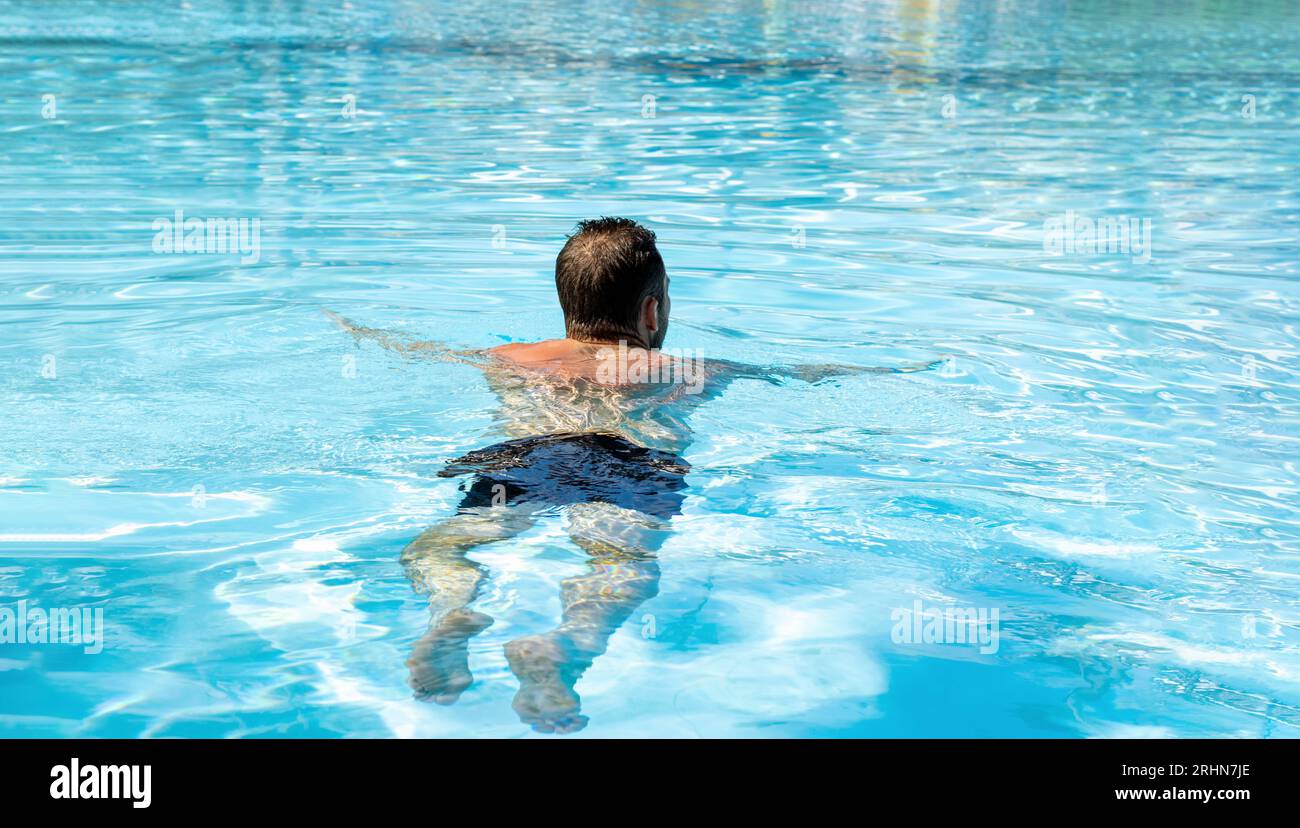 Rear view man relaxing in swimming pool during vacation in resort in ...