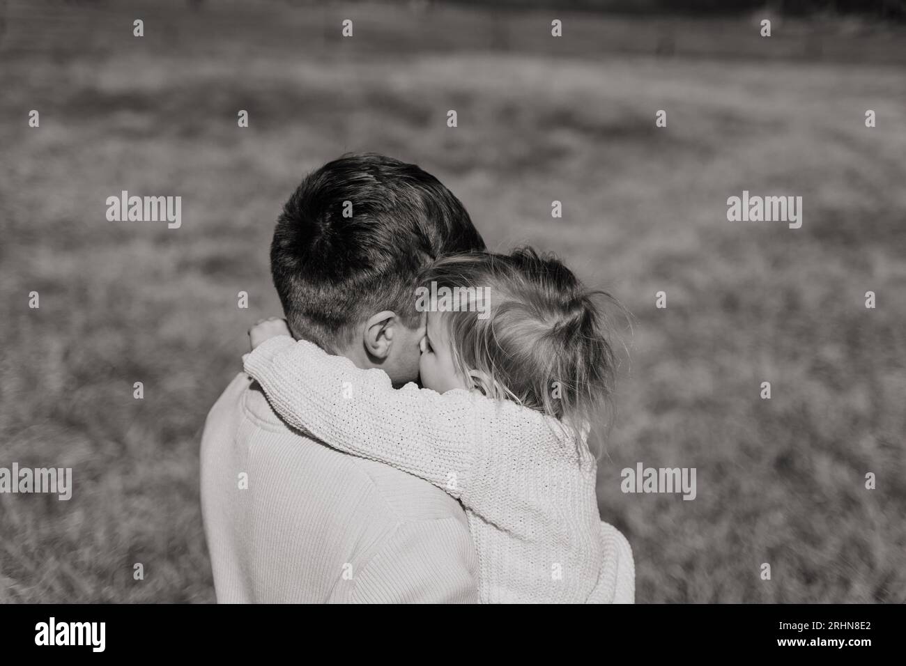 A man tightly hugs a small child in a dry field, back view, close up ...