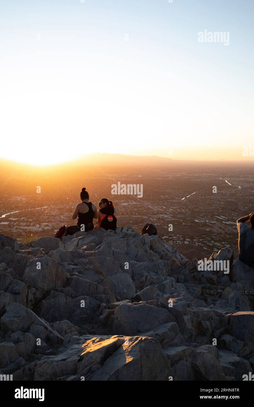 Women on rocky ledge overlooking town at sunset vertical Stock Photo ...