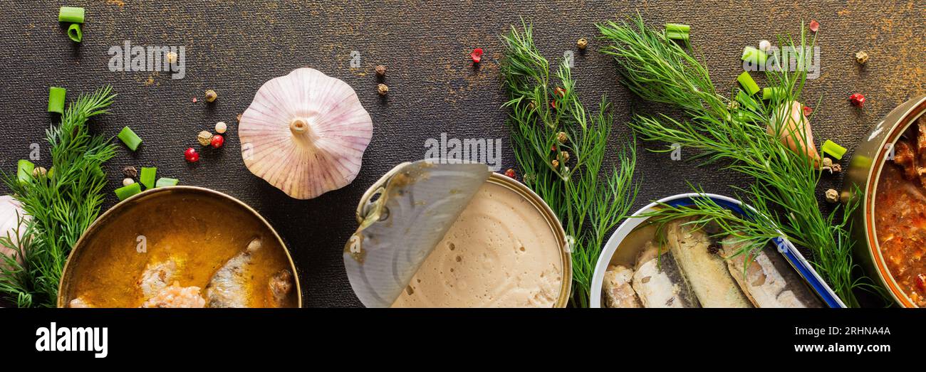 Different open tin cans with canned fish among spices and herbs banner ...
