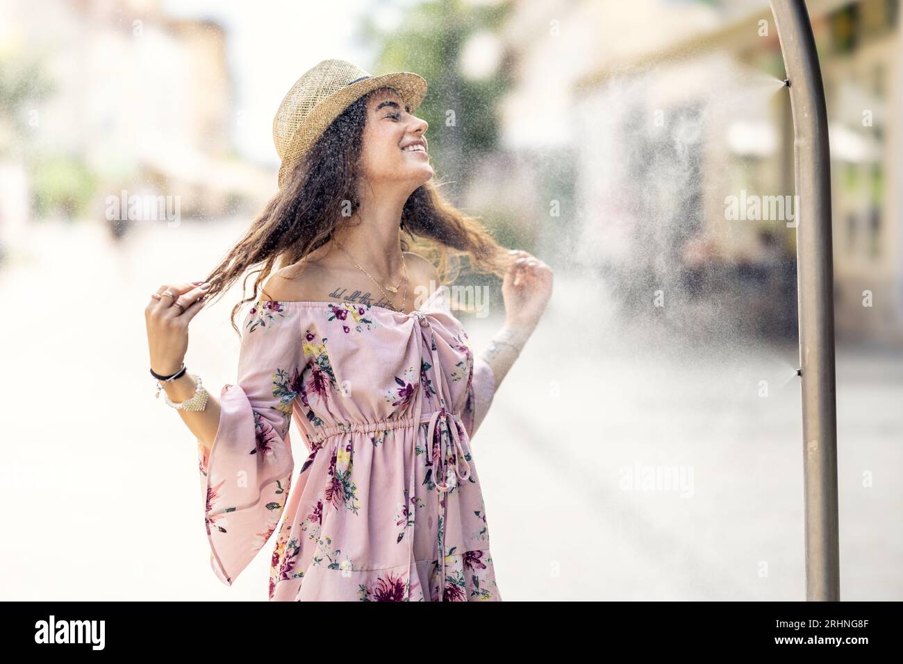 A cute young lady is relaxing from the heat under a water shower in the ...