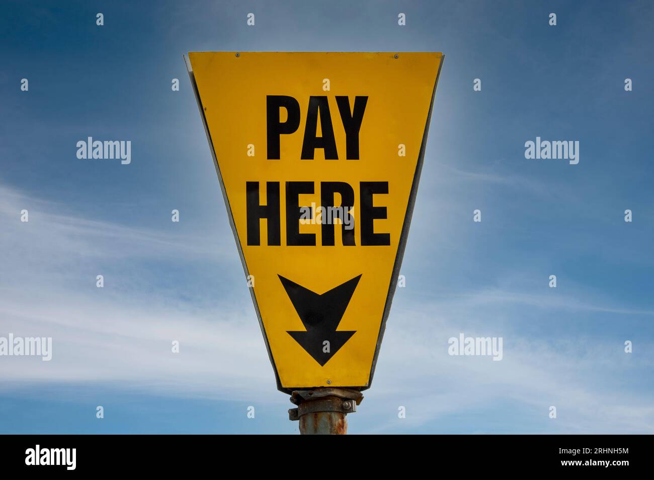 Yellow pay here sign with an arrow pointing down against a blue sky ...