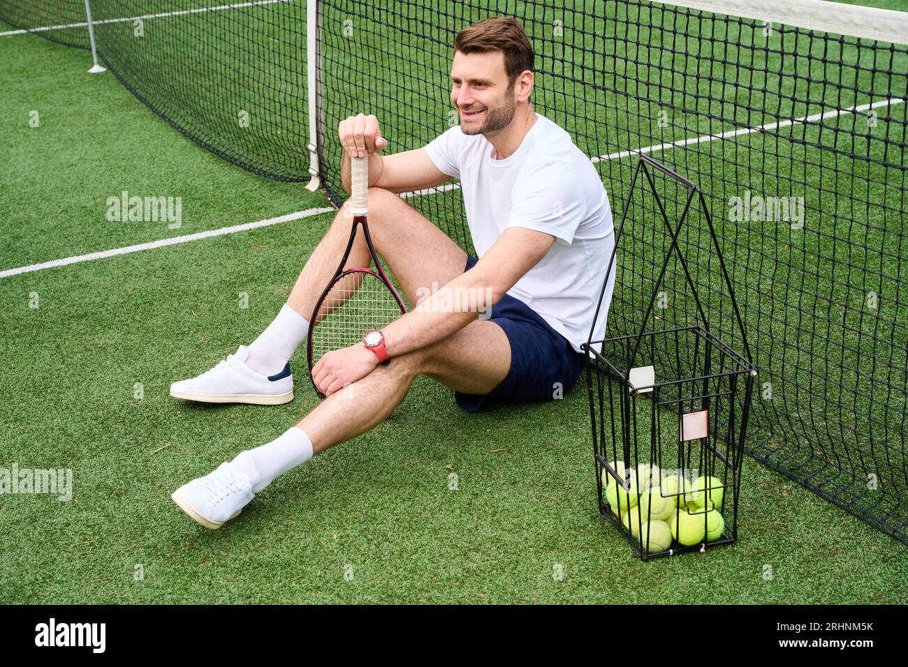 Smiling handsome man sitting on the grass on tennis court Stock Photo ...