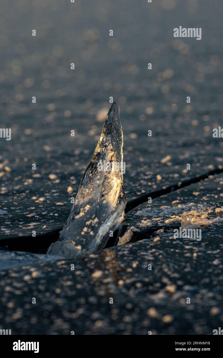 A sharp triangular piece of ice illuminated by sunset light, vertical ...