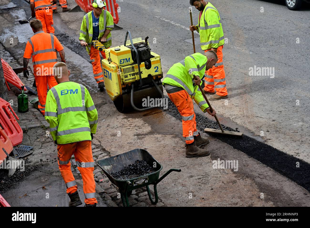 Workmen laying asphalt and compacting with vibrating roller finishing ...