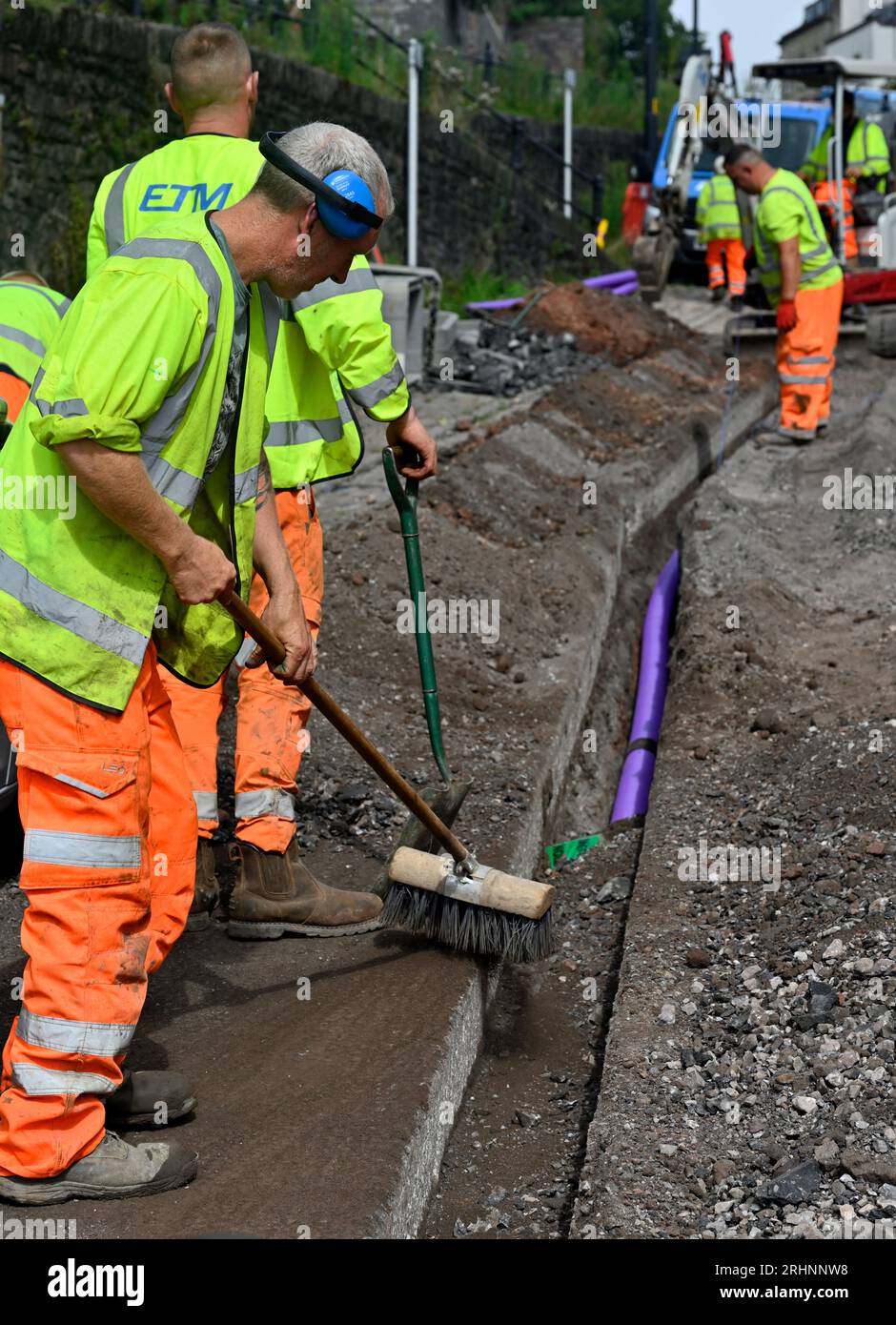 Workmen installing ducting for fibre optic cable in trench cut in road ...