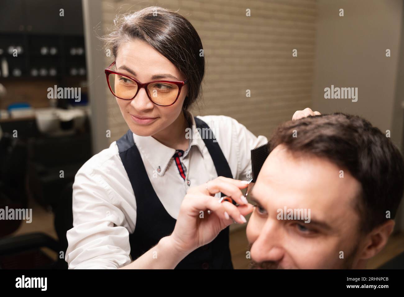 Female with glasses cuts clients hair with scissors Stock Photo - Alamy