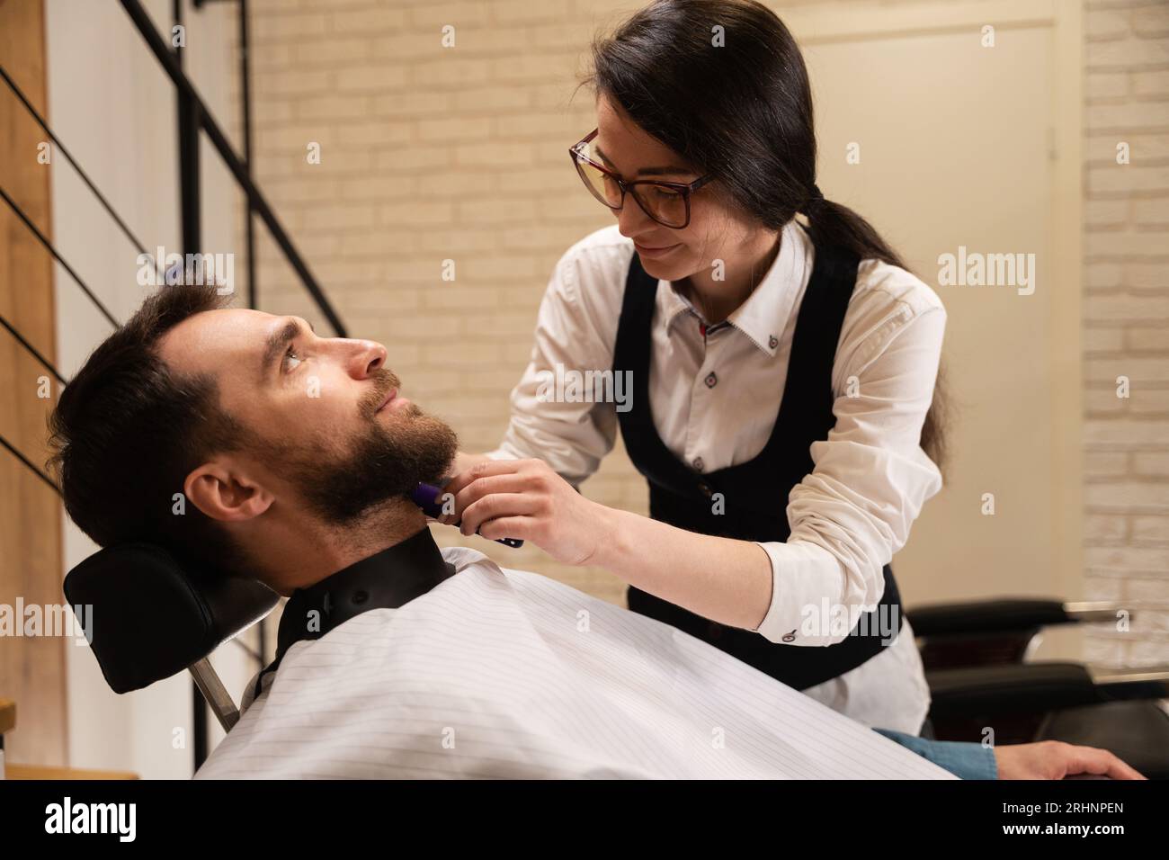 Female barber in glasses works with a clients beard Stock Photo - Alamy