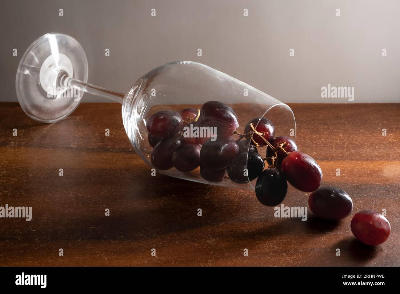 A wine glass falling on wooden table and dark red grapes flowing out ...
