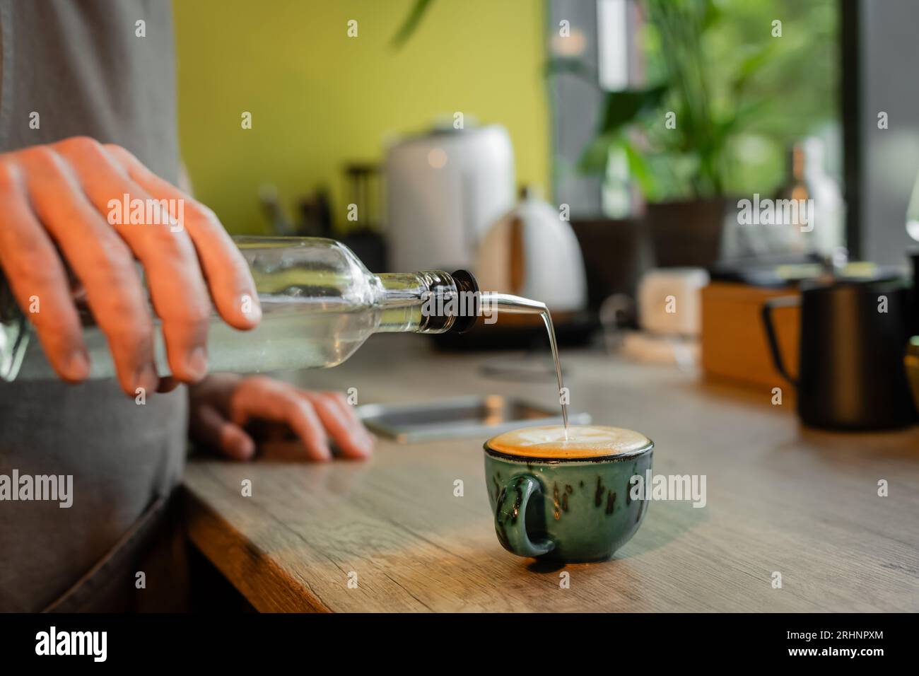 cropped view of barista pouring syrup in cup of cappuccino on worktop ...