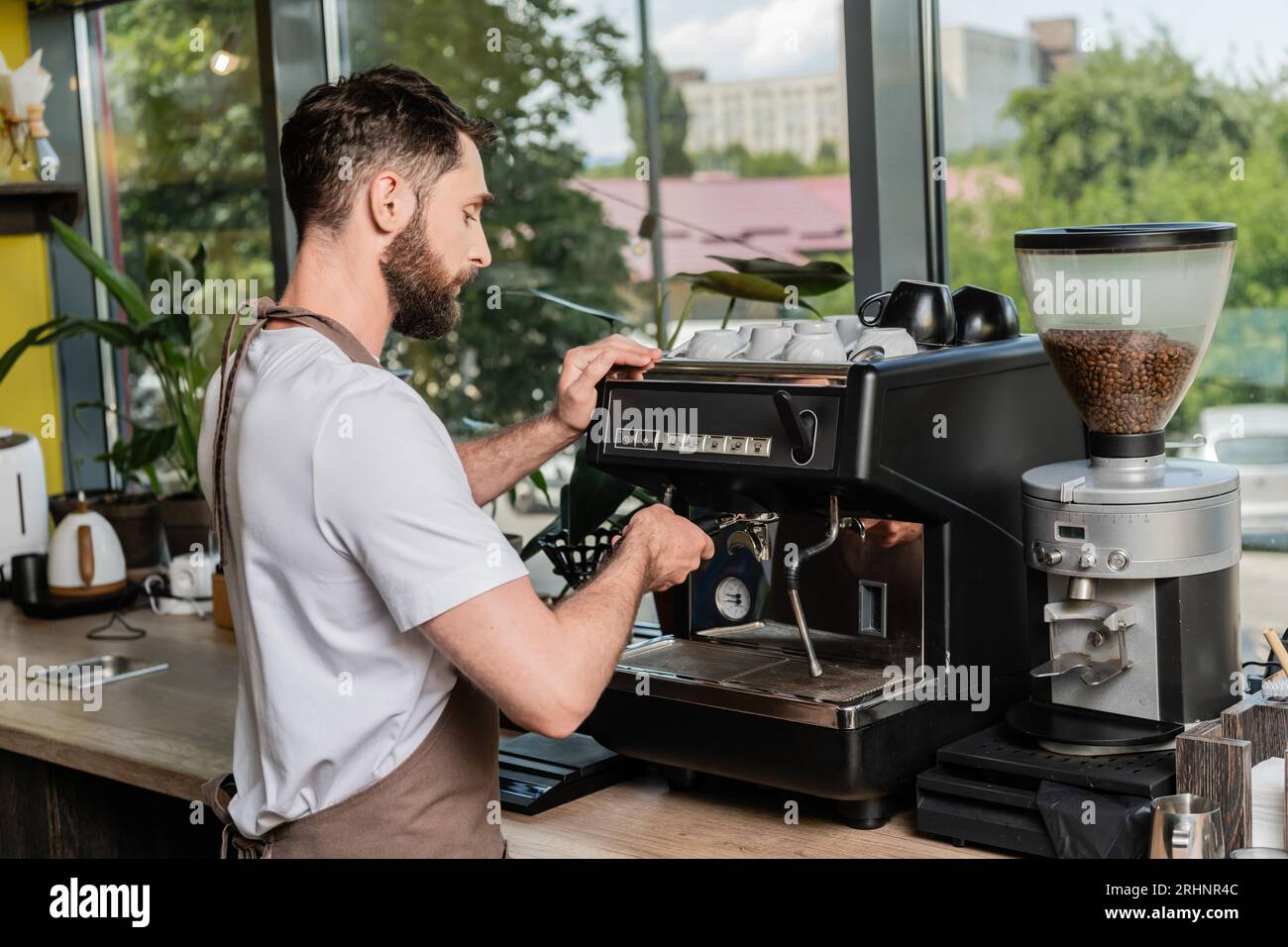 side view of bearded barista in apron working with coffee machine in ...