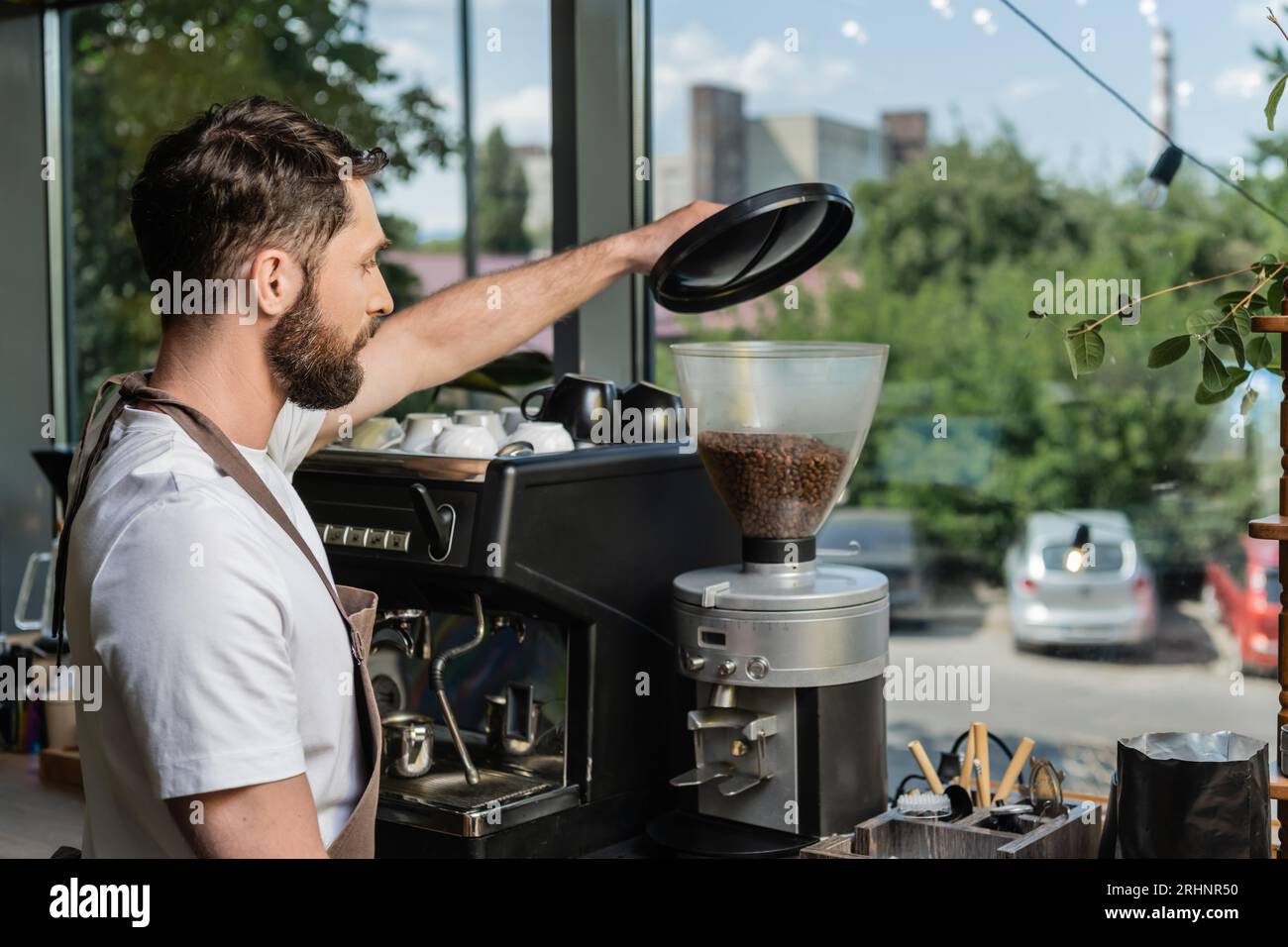 side view of barista in apron using coffee grinder while working in ...