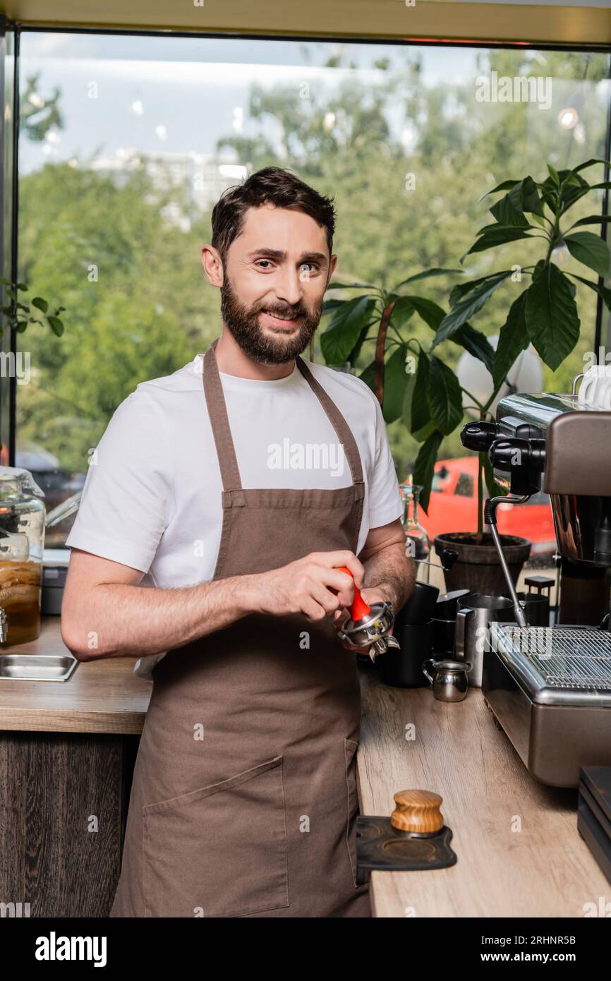 smiling barista looking at camera while holding press and coffee ...