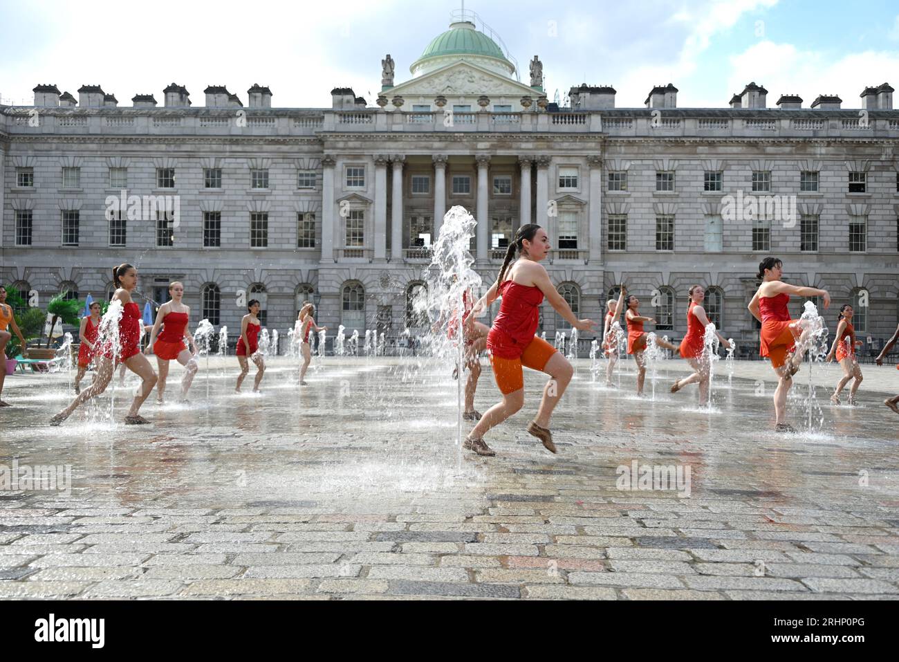 22 all-female dancers in vivid orange costumes designed by Ursula Bombshell dancing in the ...