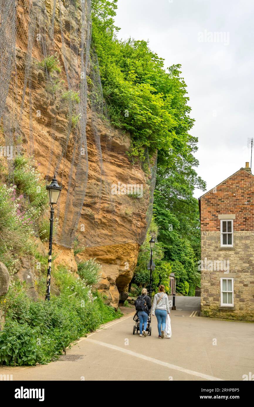 Young women walking along Waterside at bottom of cliff face Nidd Gorge ...