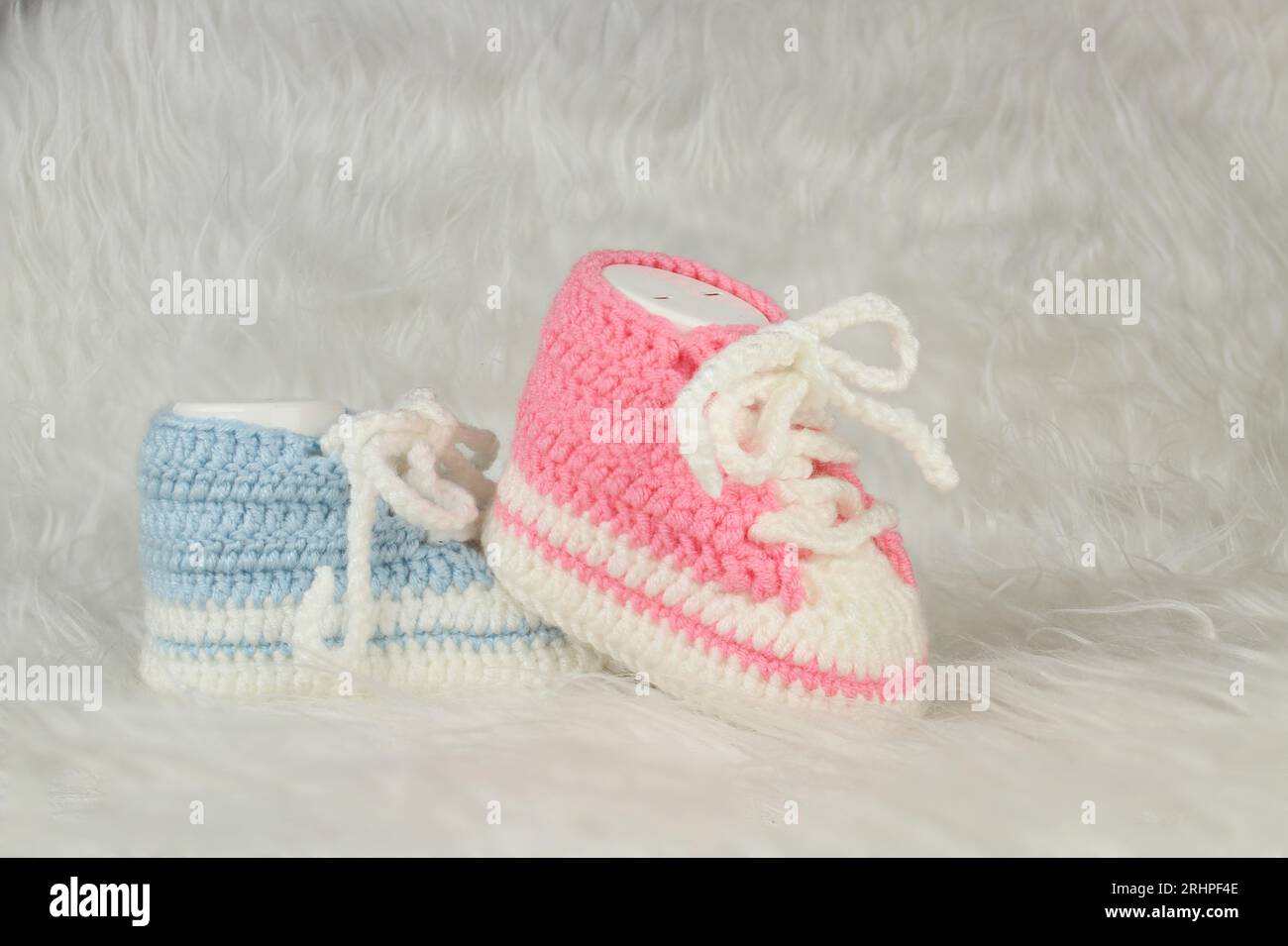 Knitted pink and blue booties on white fluffy blanket. Gender party ...