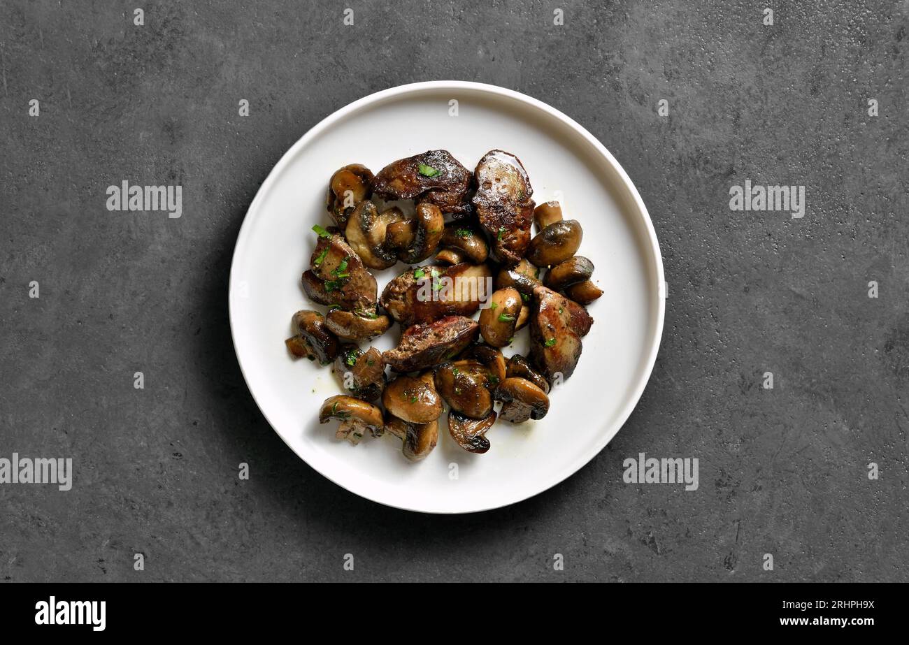 Roasted chicken liver with mushrooms on white plate over dark stone ...