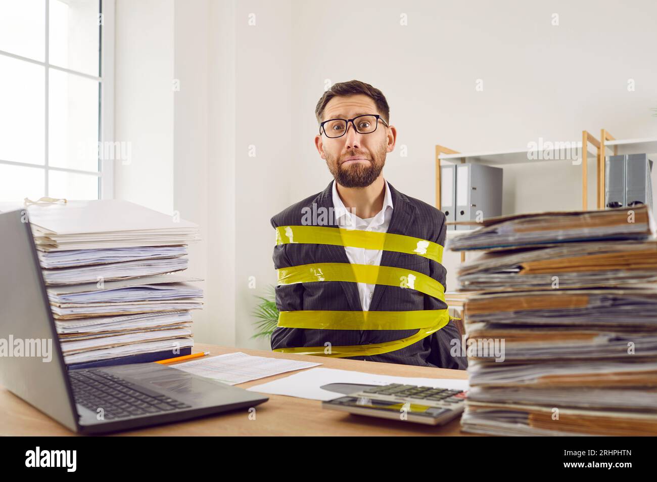 Funny, sad work slave, restrained with adhesive tape, sitting at office ...
