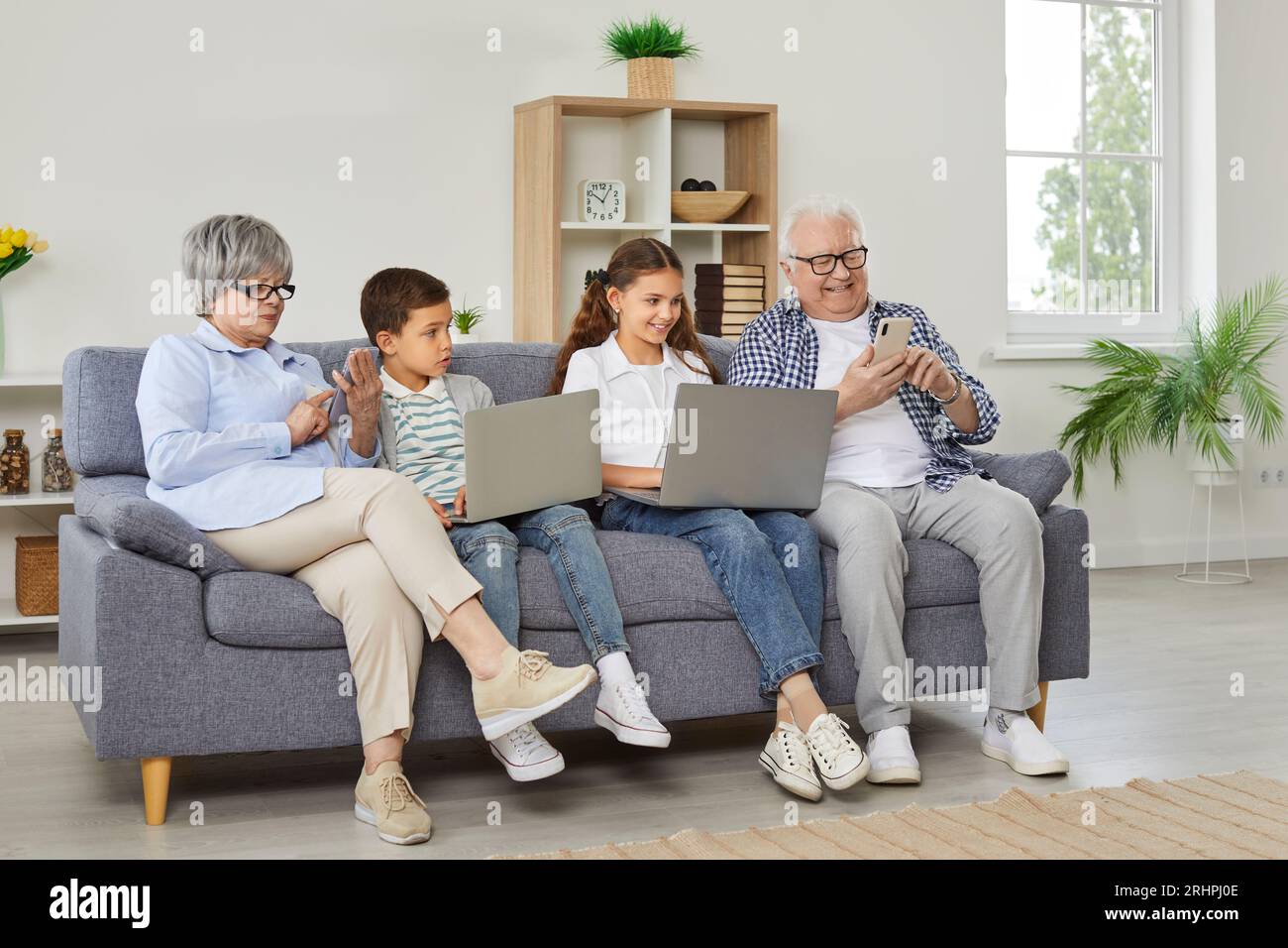 Happy grandparents with two kids sitting on the sofa using laptops and ...