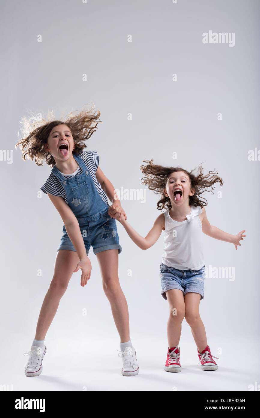 In jeans and sneakers, two girls joyfully leap and dance, hands ...