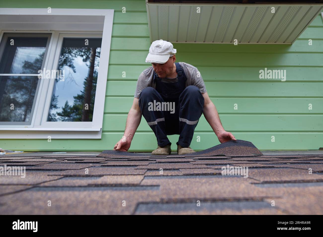 Male worker lays a sheet of soft flexible bitumen shingles on the roof ...