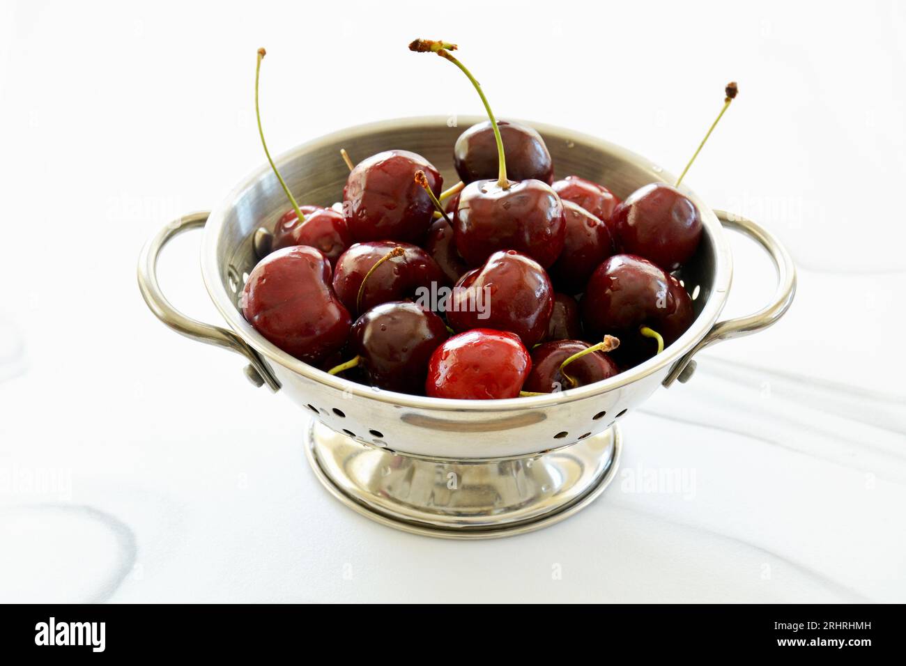 Organic fresh picked dark cherries in rustic metal colander on marble ...