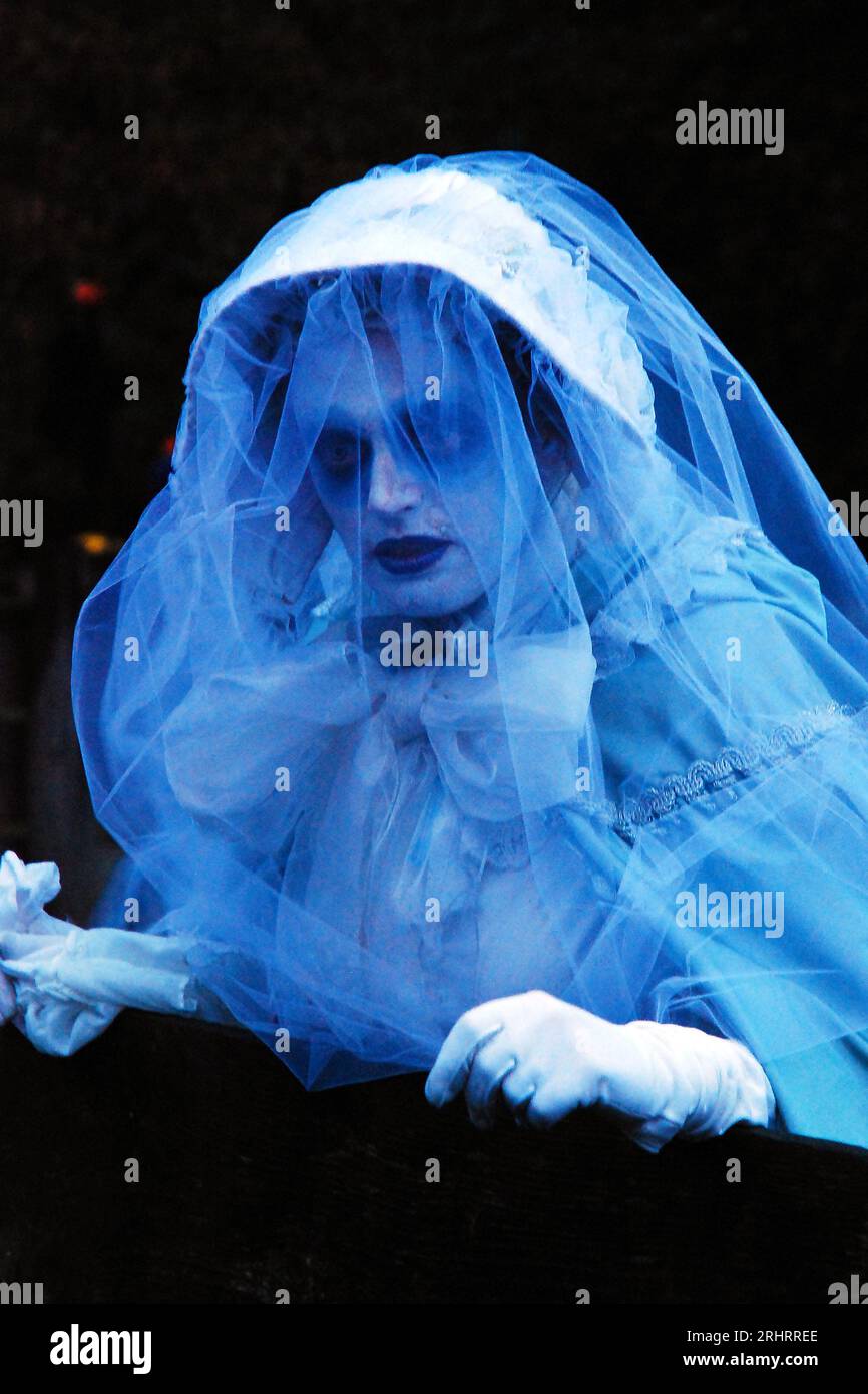 A young woman dresses up as a ghost in a bridal gown and veil costume ...