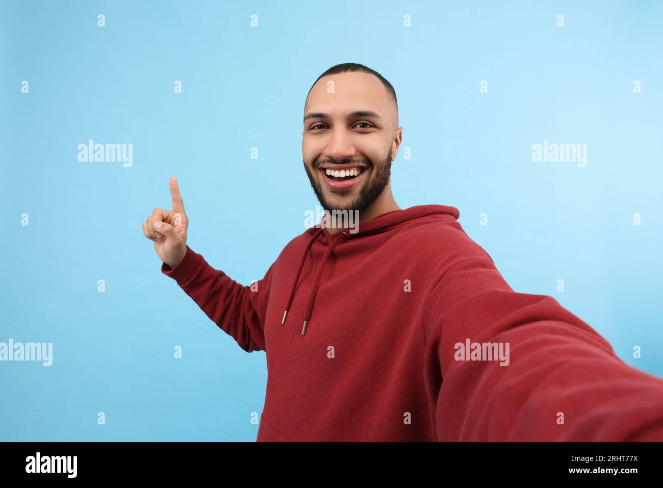 Smiling young man taking selfie on light blue background Stock Photo ...
