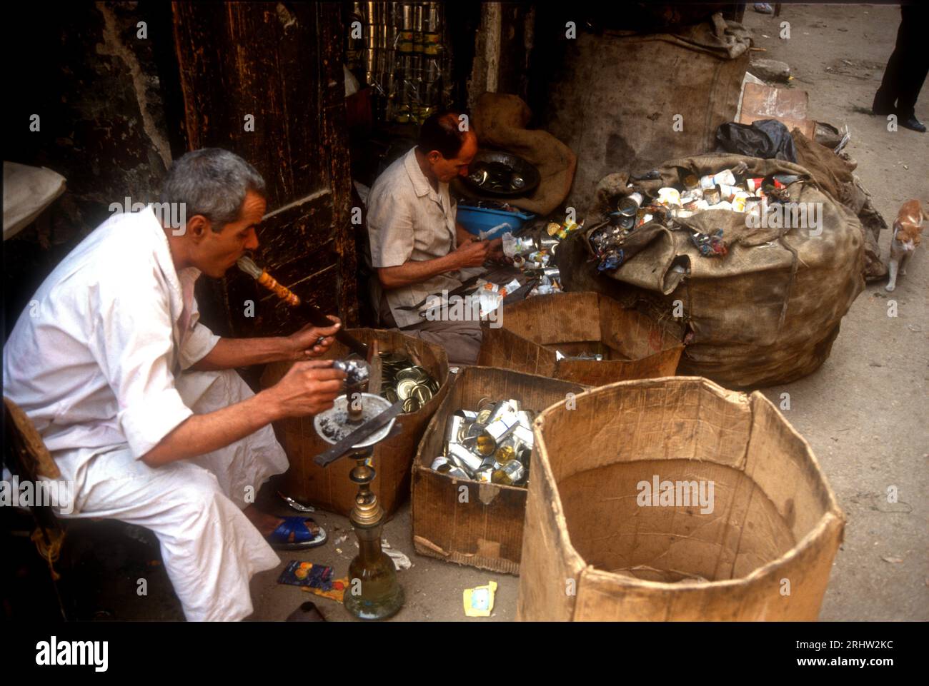 Men sorting used glass items for recycling. One is smoking a hookah, or ...