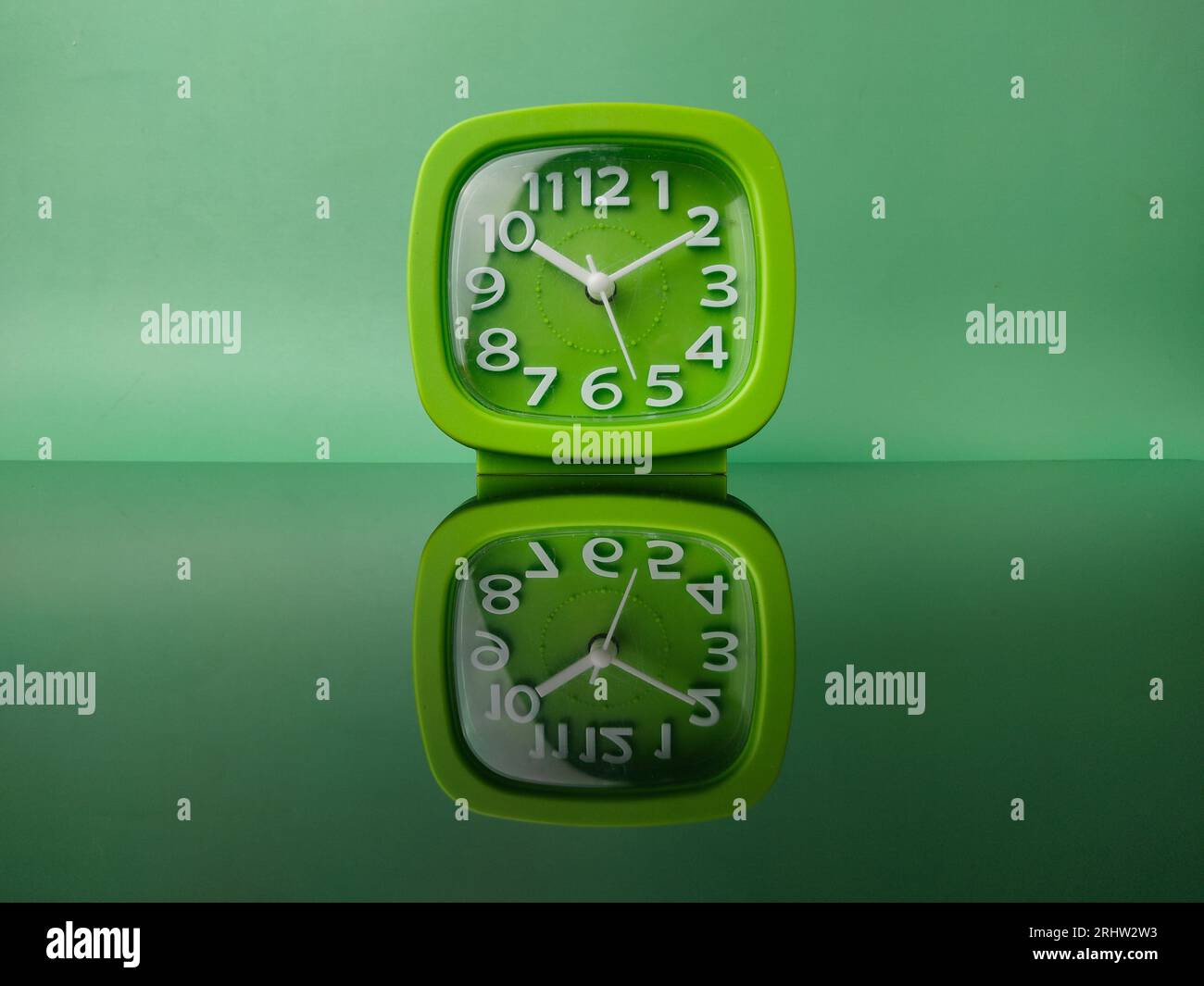 Green clock on green background with reflection on a black acrylic ...